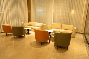Espaço de convivência moderno com sofá bege, duas poltronas e uma mesa de centro.