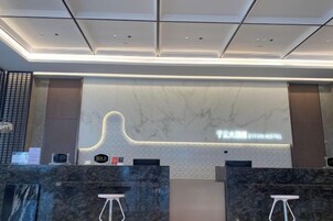 Uma área de recepção de hotel com balcão de mármore, relógio digital e espaço para acomodação.