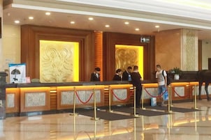 Uma área de recepção de hotel com balcão, sala de espera e painel decorativo.