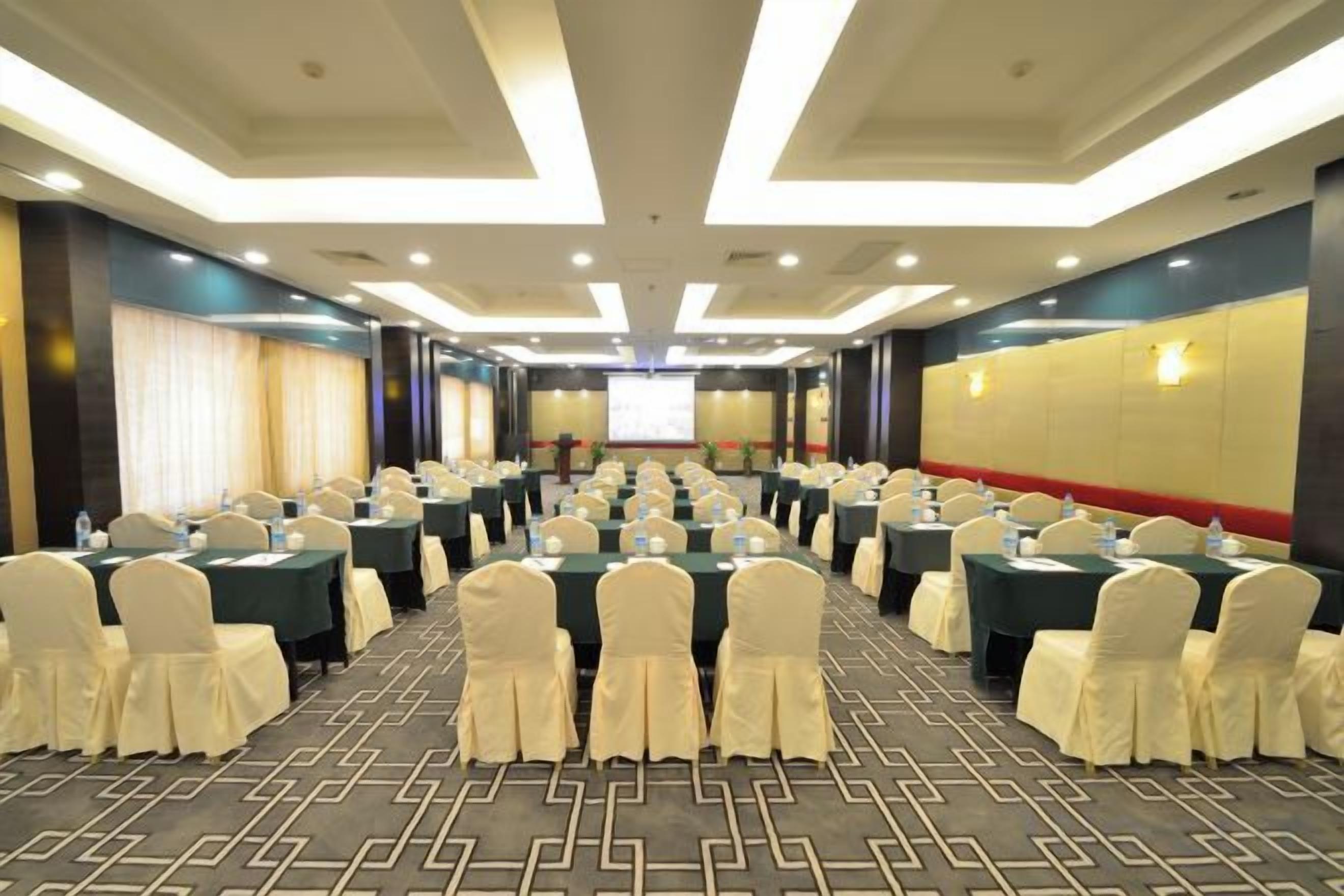 Sala de conferência com mesas e cadeiras dispostas em fileiras, equipada com garrafas de água e placas de identificação.