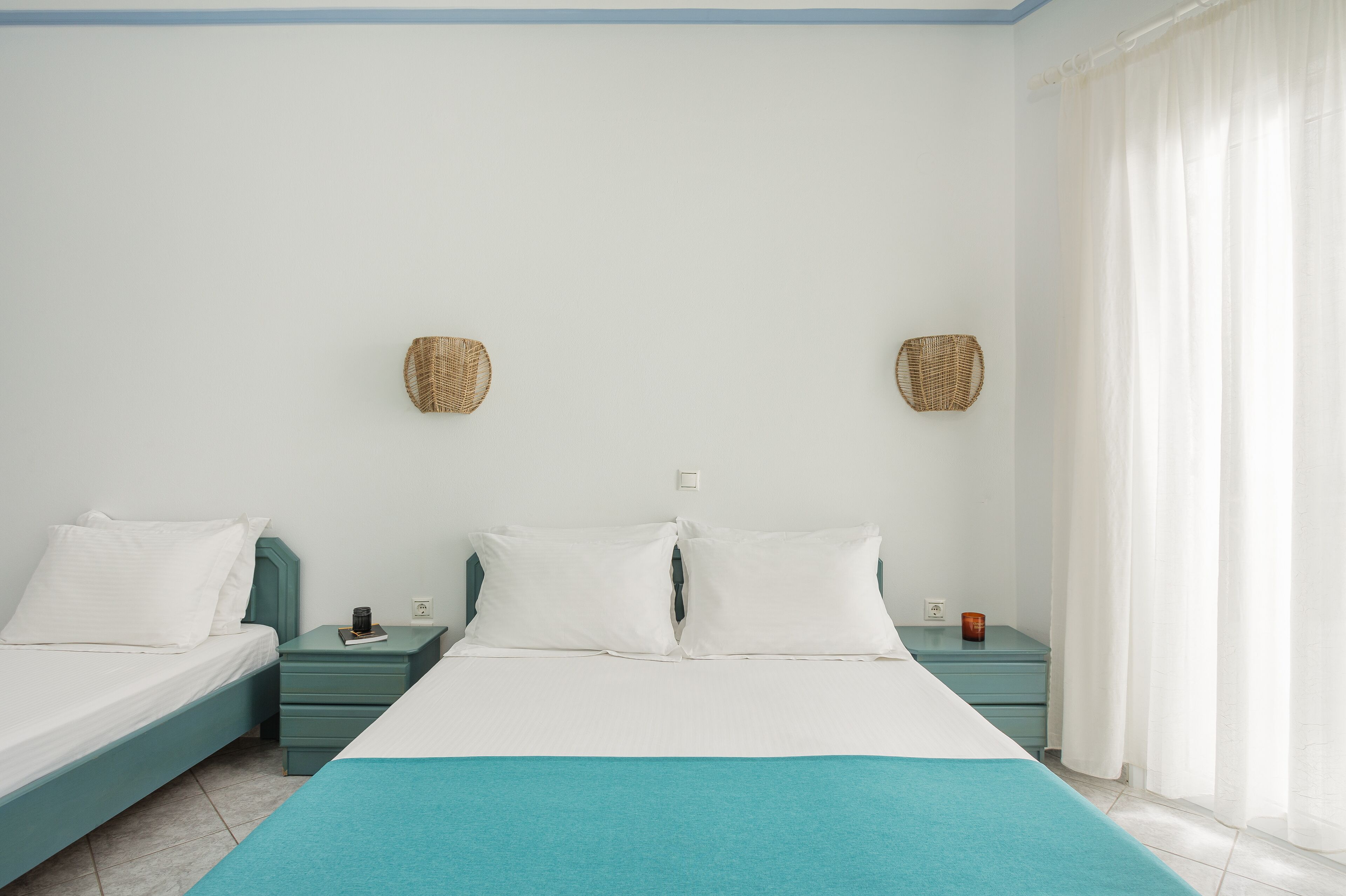 Quarto com duas camas, um cobreleira azul-turquesa e duas mesinhas de cabeceira com cestos de vime.