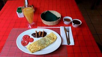 Refeição com omelete, tomate e uma bebida sobre uma toalha vermelha.