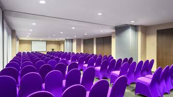 Uma sala de conferências com fileiras de cadeiras roxas e uma tela de projeção na frente.