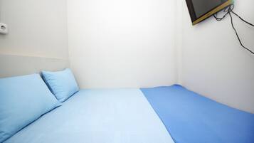 Uma cama de solteiro com roupa de cama azul num quarto com paredes brancas.