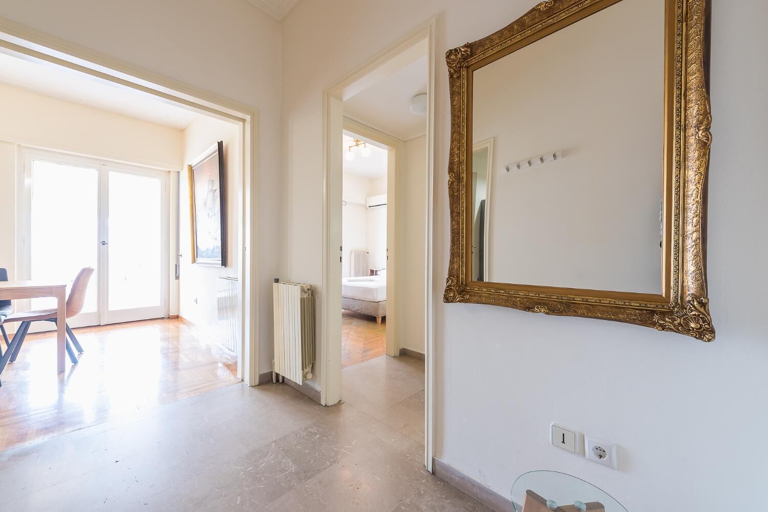 Um quarto espaçoso com um espelho grande, um radiador e uma porta que dá para outro quarto.