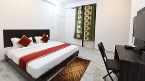 Quarto de hotel com cama, escrivaninha, cadeira, televisão e janela com cortinas.