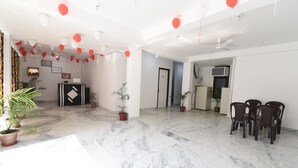 Um hall amplo com piso de mármore, balcão de recepção, plantas em vasos e área de refeições com cadeiras.