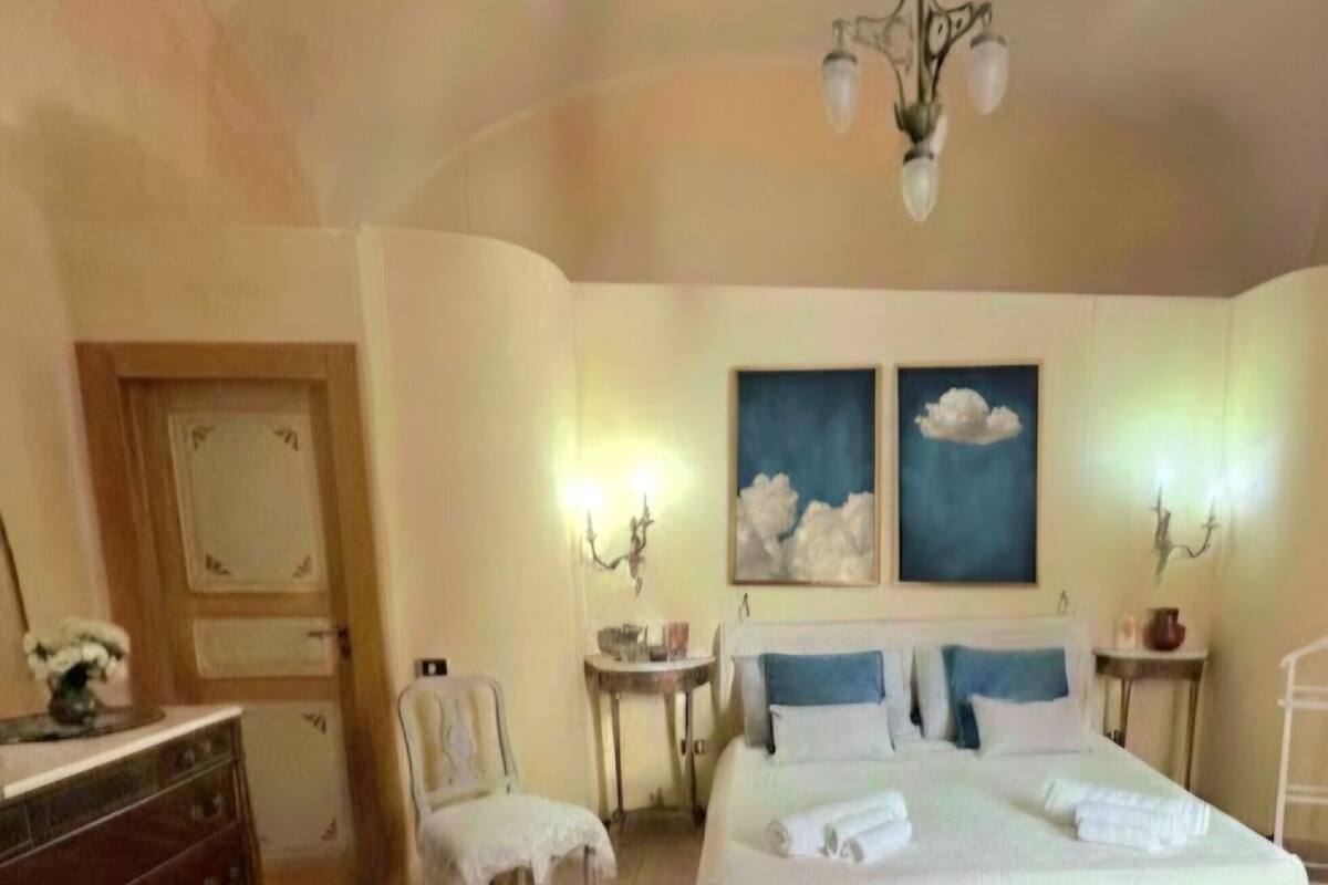 Quarto com cama, mesas de cabeceira, uma cadeira, cômoda e luminária de teto.