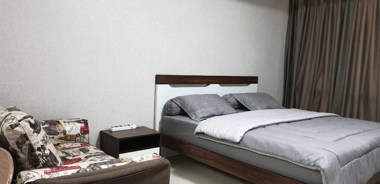 Um quarto com cama, mesa de cabeceira, cadeira e cortina.