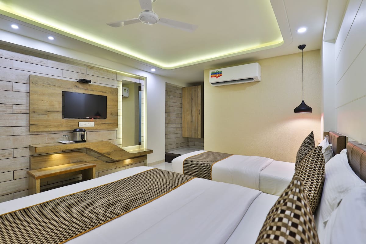 Quarto de hotel com duas camas, televisão, ventoinha de teto e ar condicionado.