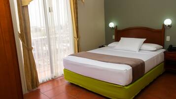 Quarto de hotel com cama, cortinas, mesa de cabeceira e luminária fixada na parede.