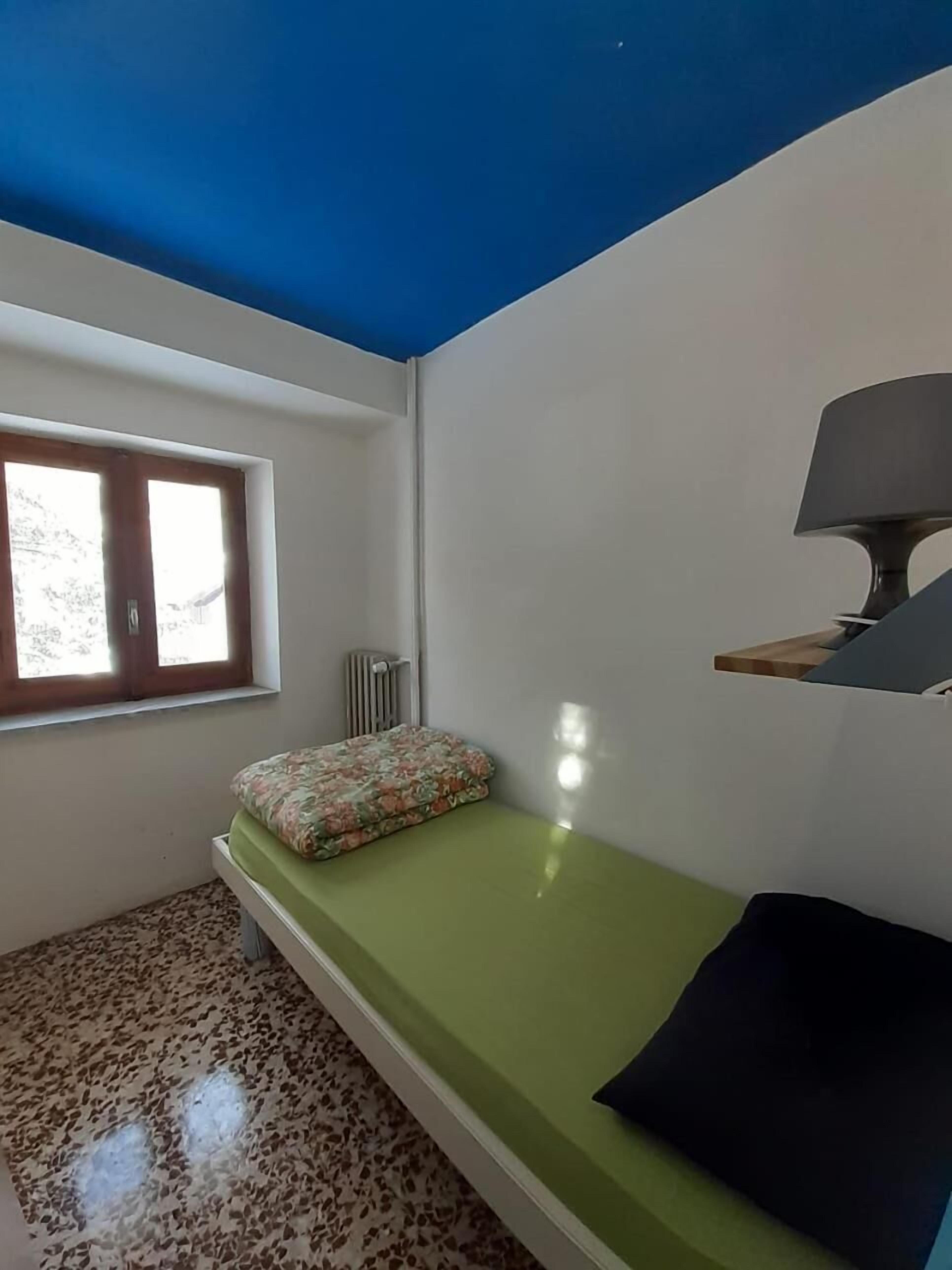 Quarto pequeno com uma cama de solteiro, janela e radiador.