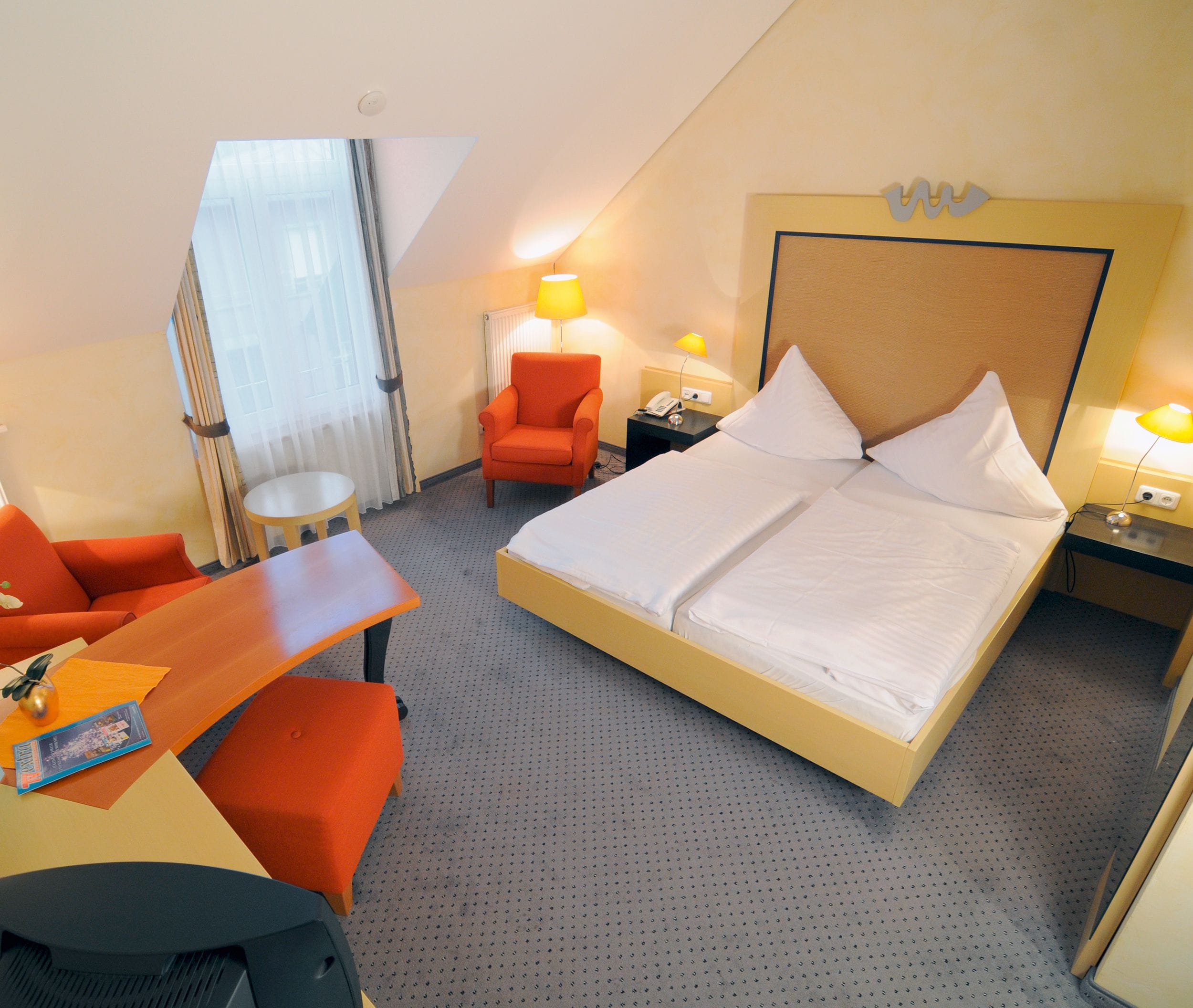 Quarto de hotel com uma cama, uma cadeira, uma mesa e uma luminária.