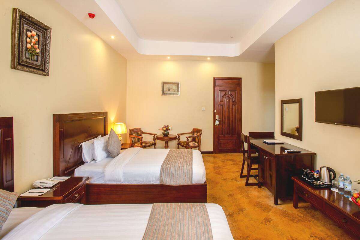 Quarto de hotel com duas camas, uma escrivaninha, uma cadeira, uma televisão e uma fruteira.