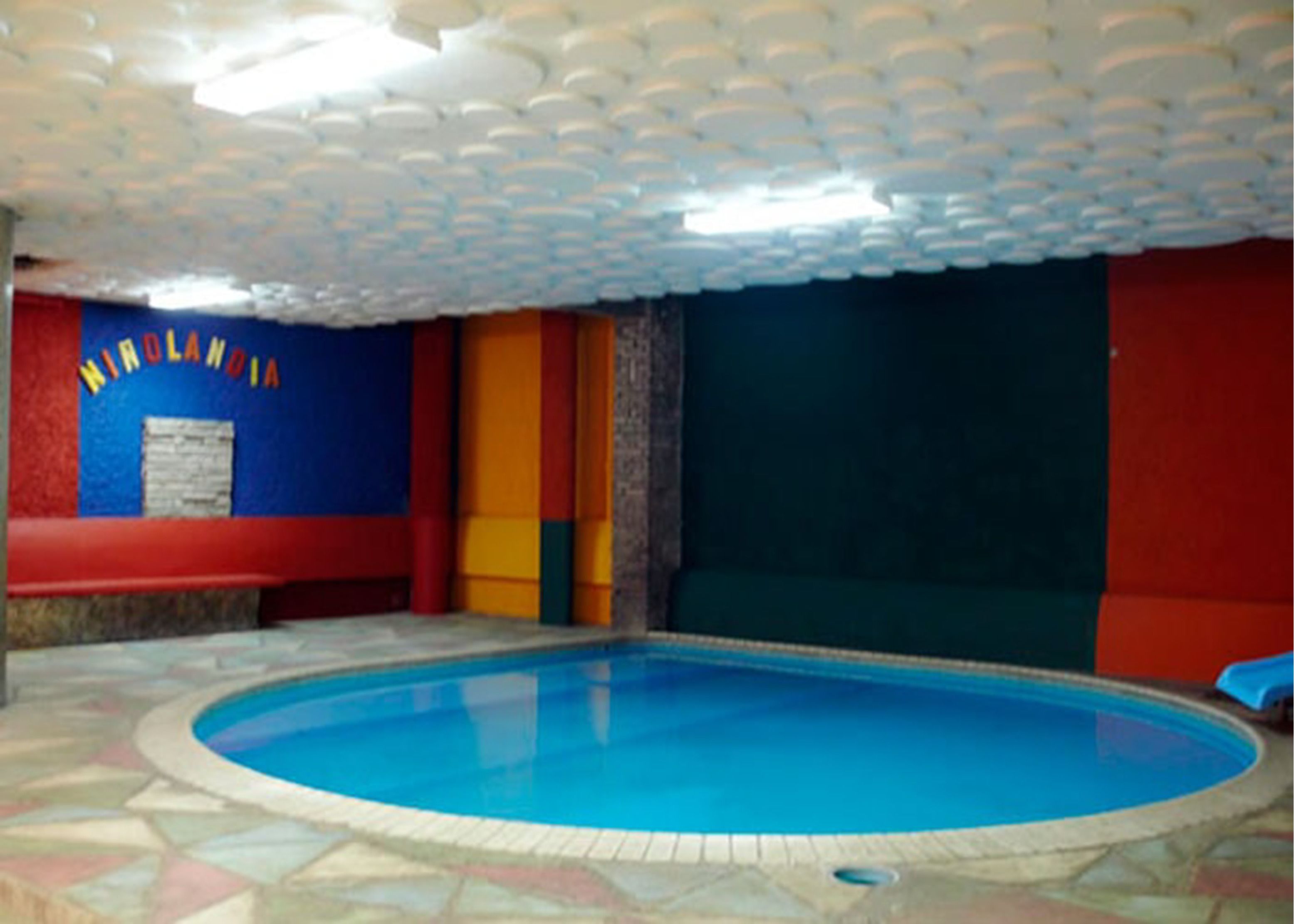 Piscina interior com destaque para o azul da água, rodeada por um chão e paredes com azulejos coloridos.