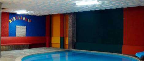 Piscina interior com destaque para o azul da água, rodeada por um chão e paredes com azulejos coloridos.