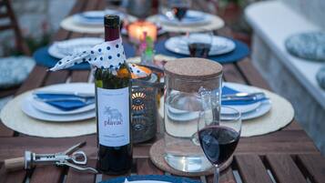 Mesa posta com pratos, talheres, garrafa de vinho, abridor de garrafa, taça de vinho tinto, vela e um lança-lume decorativo.