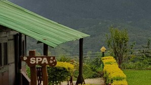 Um sinal de spa, um edifício com telhado verde e um jardim paisagístico com flores amarelas e montanhas ao fundo.