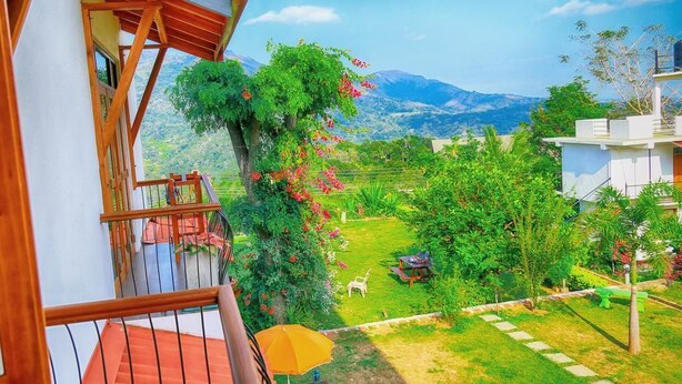 Varanda com guarda-corpo de madeira, vista para um jardim exuberante com montanhas ao fundo.