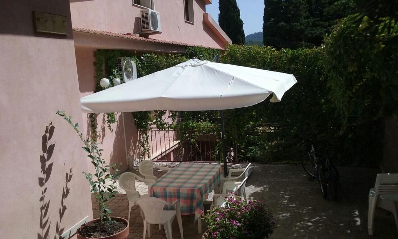 Um pátio externo com uma mesa, cadeiras, um guarda-sol branco e um vaso com planta.