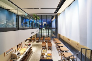 Espaçoso espaço interno com várias mesas e cadeiras, um serviço de buffet e grandes janelas com vista para a paisagem urbana.
