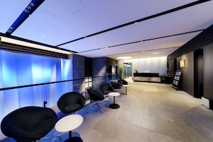 Uma área de recepção moderna com balcão, cadeiras pretas e guarda-corpo de vidro.