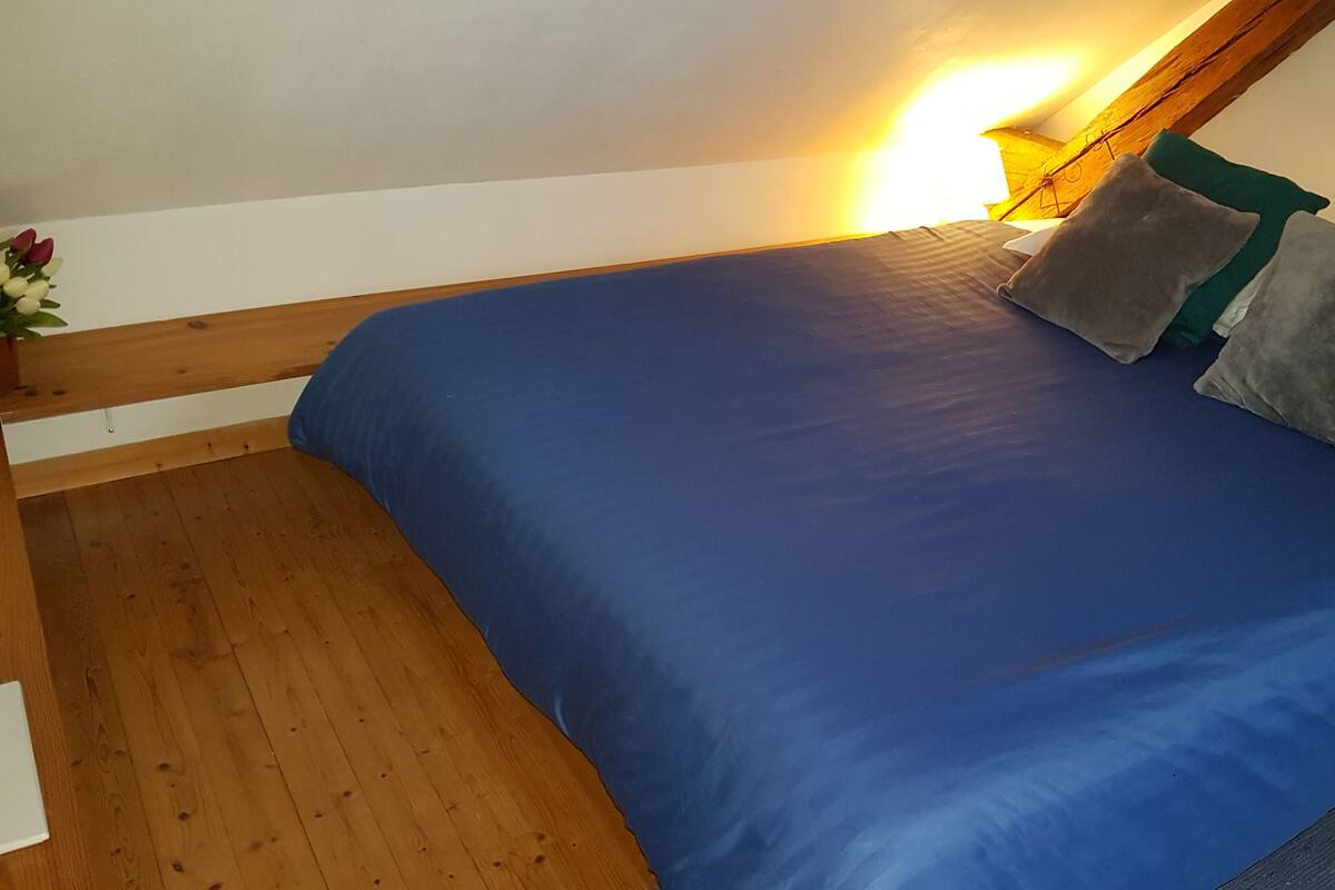 Quarto com colcha azul, piso de madeira e uma luminária de cabeceira.