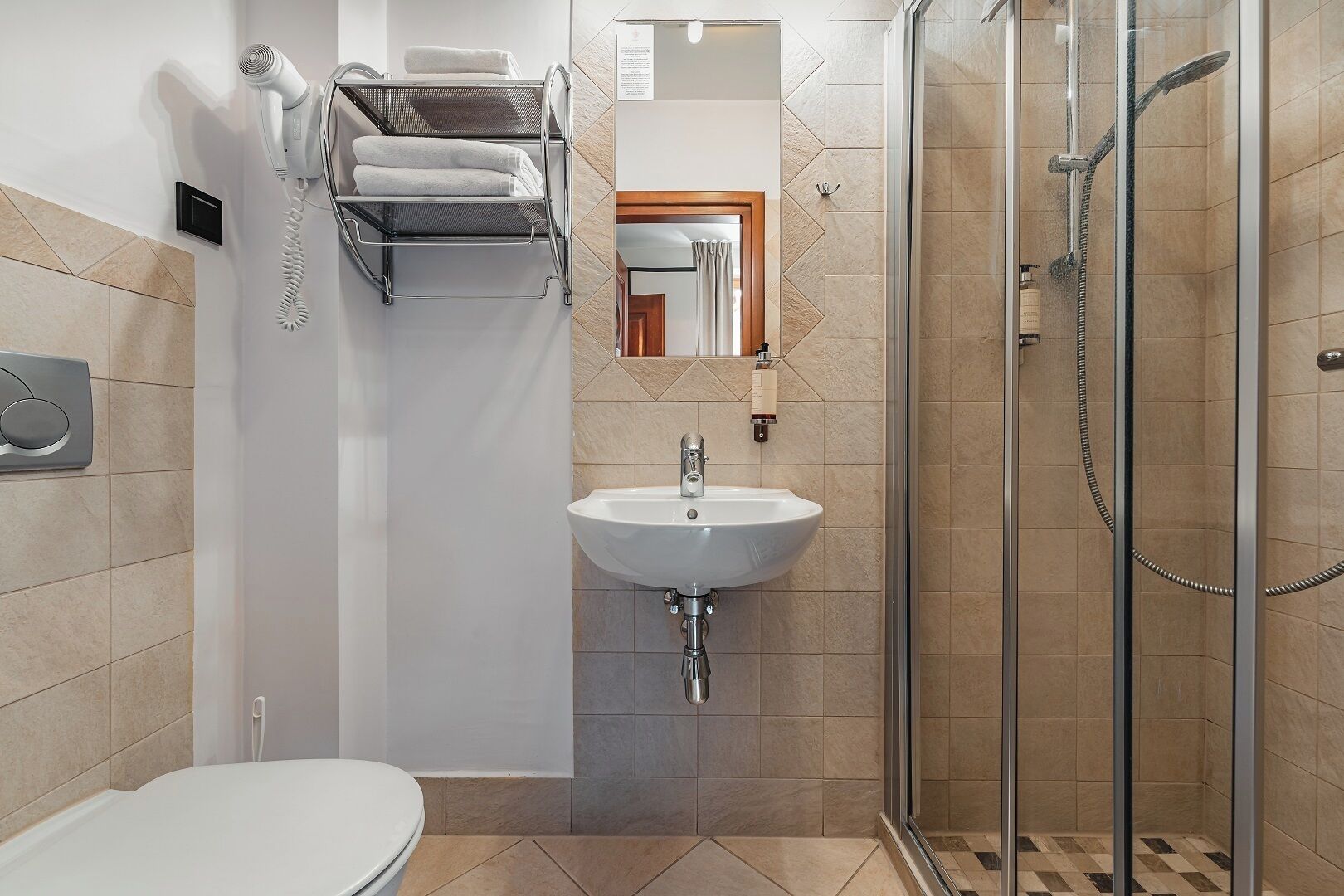 Uma casa de banho com uma pia branca, uma cabine de duche envidraçada, um porta-toalhas com toalhas dobradas e um espelho sobre a pia.