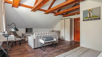 Um quarto acolhedor estilo loft com pé direito alto, vigas de madeira, sofá xadrez, pequena mesa de jantar e televisão.