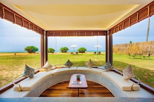 Área de estar com assentos curvos e uma mesa, com vista para um espaço ao ar livre gramado com guarda-sóis e cadeiras.
