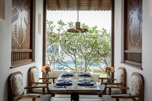 Mesa de jantar posta para quatro pessoas, vista para o mar e vegetação.