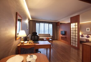 Quarto de hotel com escrivaninha, cadeira, sofá e televisão.