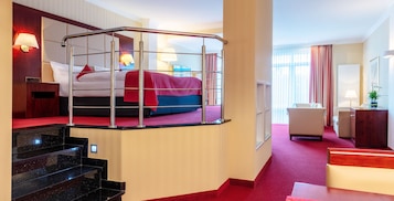 Quarto de hotel com cama beliche, escrivaninha, cadeira, luminária e janela com cortinas.