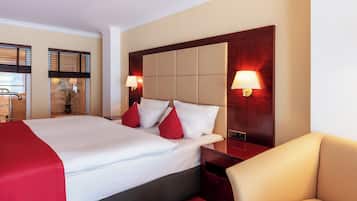 Quarto de hotel com uma cama grande, duas luminárias de cabeceira, um cobertor vermelho e uma cabeceira de madeira.