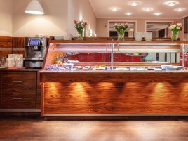 Uma área de buffet com máquina de café, diversos alimentos e uma vitrine de vidro.