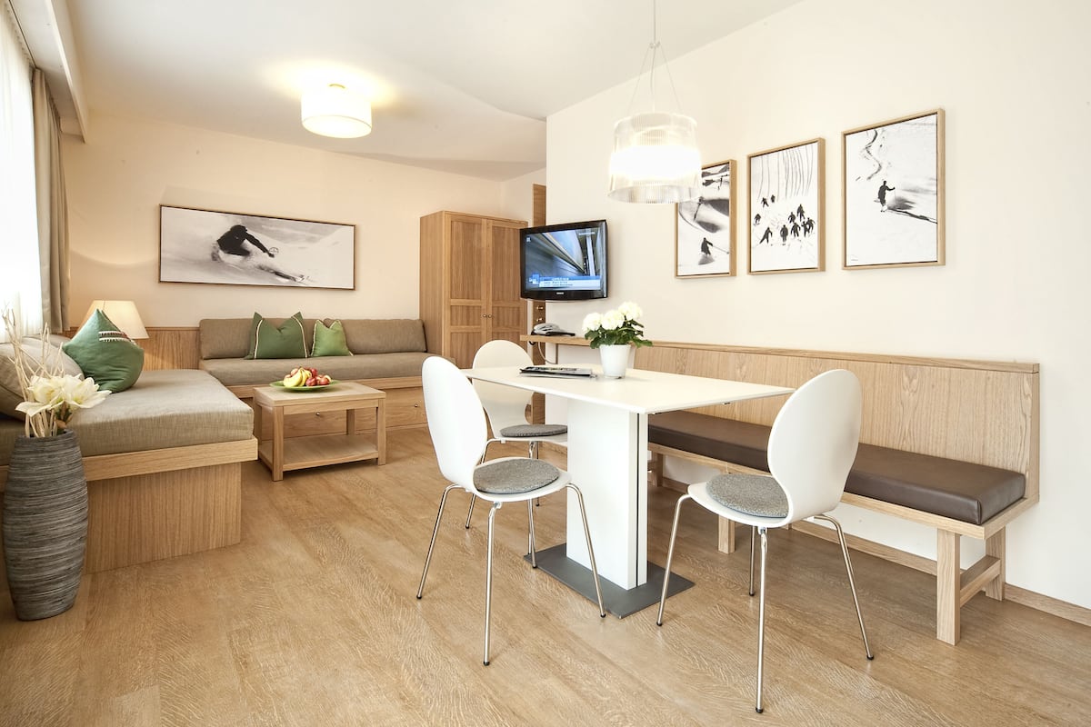 Uma sala de estar moderna com um sofá, uma mesa de jantar com cadeiras, uma televisão e obras de arte na parede.