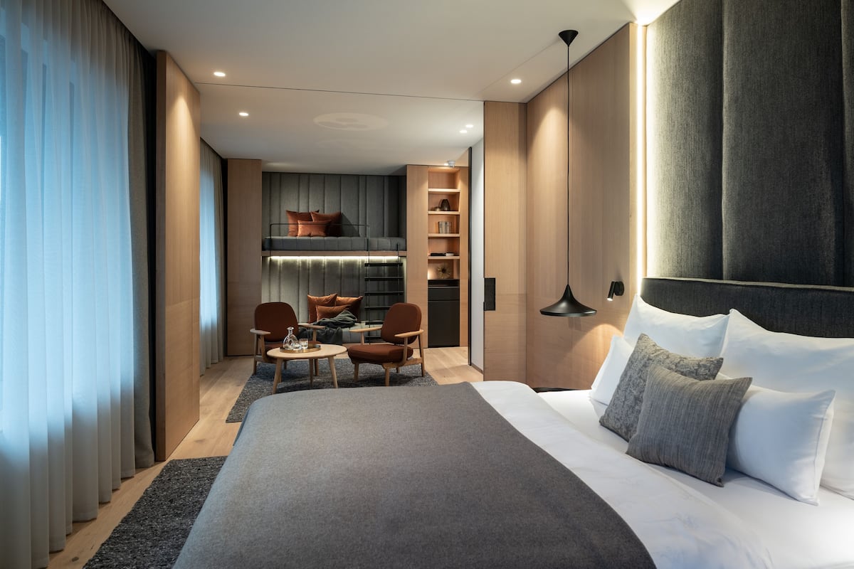 Quarto de hotel moderno com uma cama grande, uma mesa com cadeiras, uma kitchenette e um guarda-roupa.