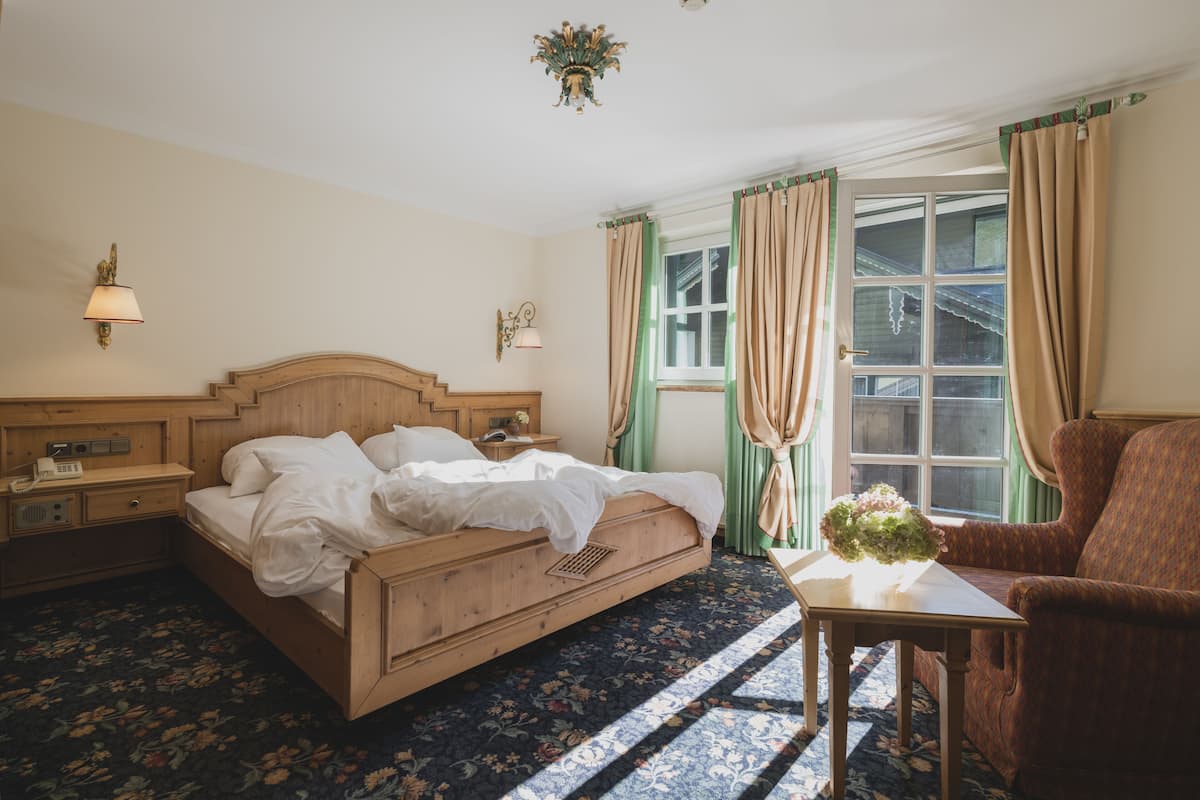 Quarto de hotel com cama de madeira, mesa de cabeceira, uma mesa com um vaso e uma cadeira.