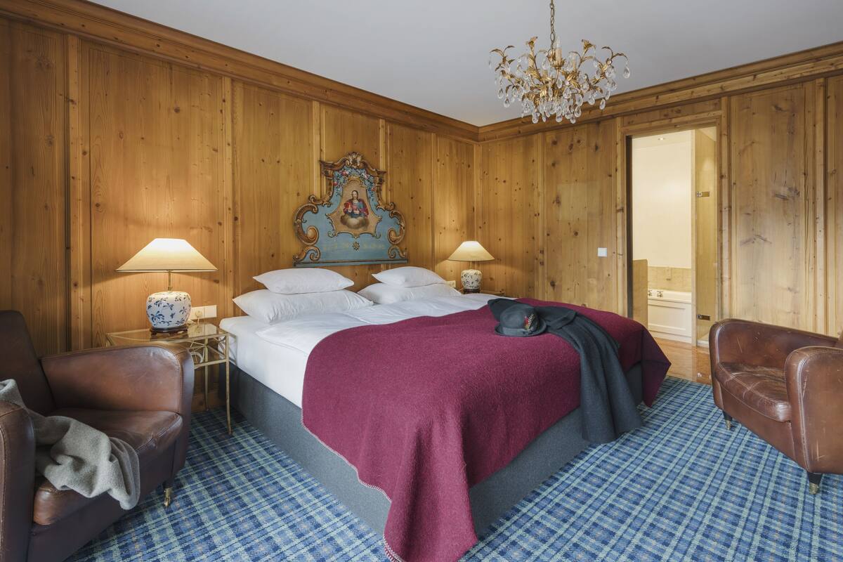 Um quarto com painéis de madeira, uma cama, duas luminárias, um lustre e um chão quadriculado em azul e branco.