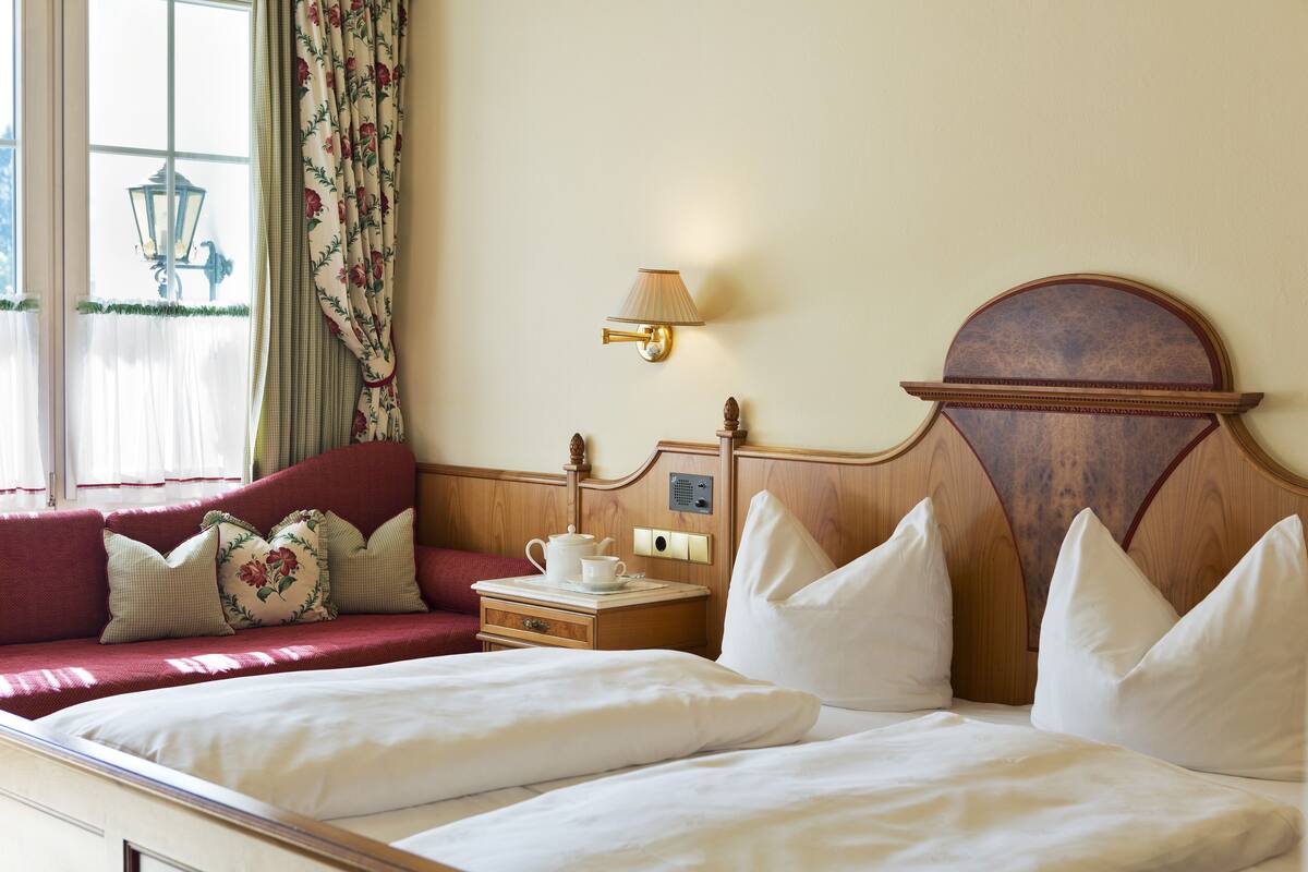 Quarto de hotel com uma cama, mesa de cabeceira, luminária, janela com cortinas e luminária fixada na parede.