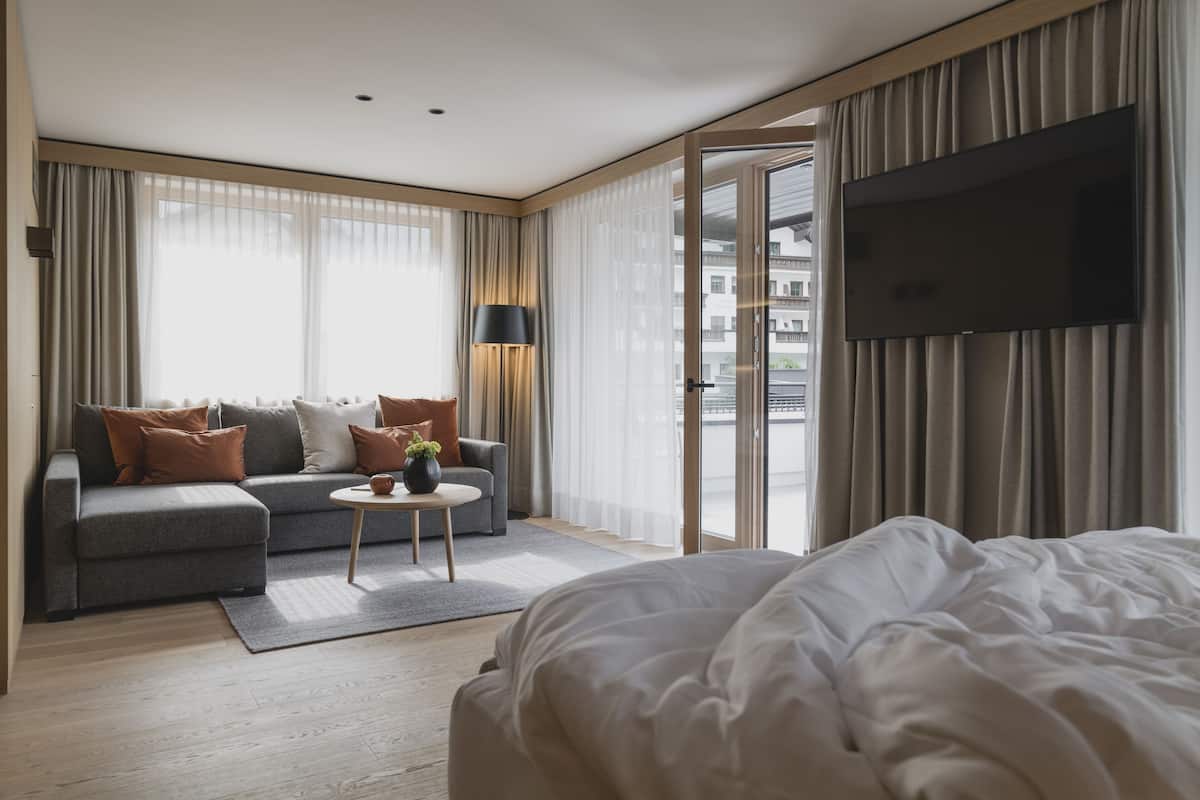 Quarto de hotel moderno com sofá, uma pequena mesa, cama e televisão.