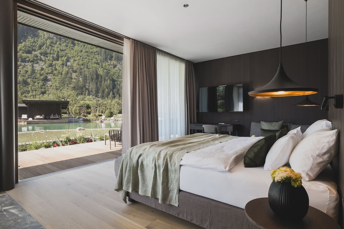 Quarto moderno com uma cama grande, vista para um lago e um espaço de refeições com mesa e cadeiras.
