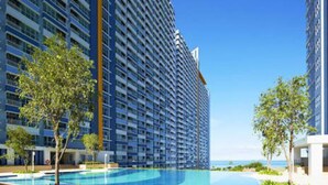 Um hotel moderno com uma grande área de piscina, rodeado por vegetação e vista clara para o oceano.