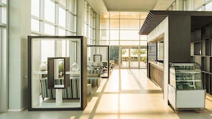 Corredor moderno de hotel com portas de vidro,  área de estar e vitrine refrigerada.