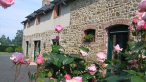 Um edifício de pedra com porta verde e janelas, rodeado por rosas cor-de-rosa.