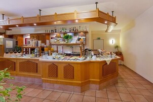 Disposição de buffet com diversos alimentos e bebidas, um balcão de madeira e teto decorativo.