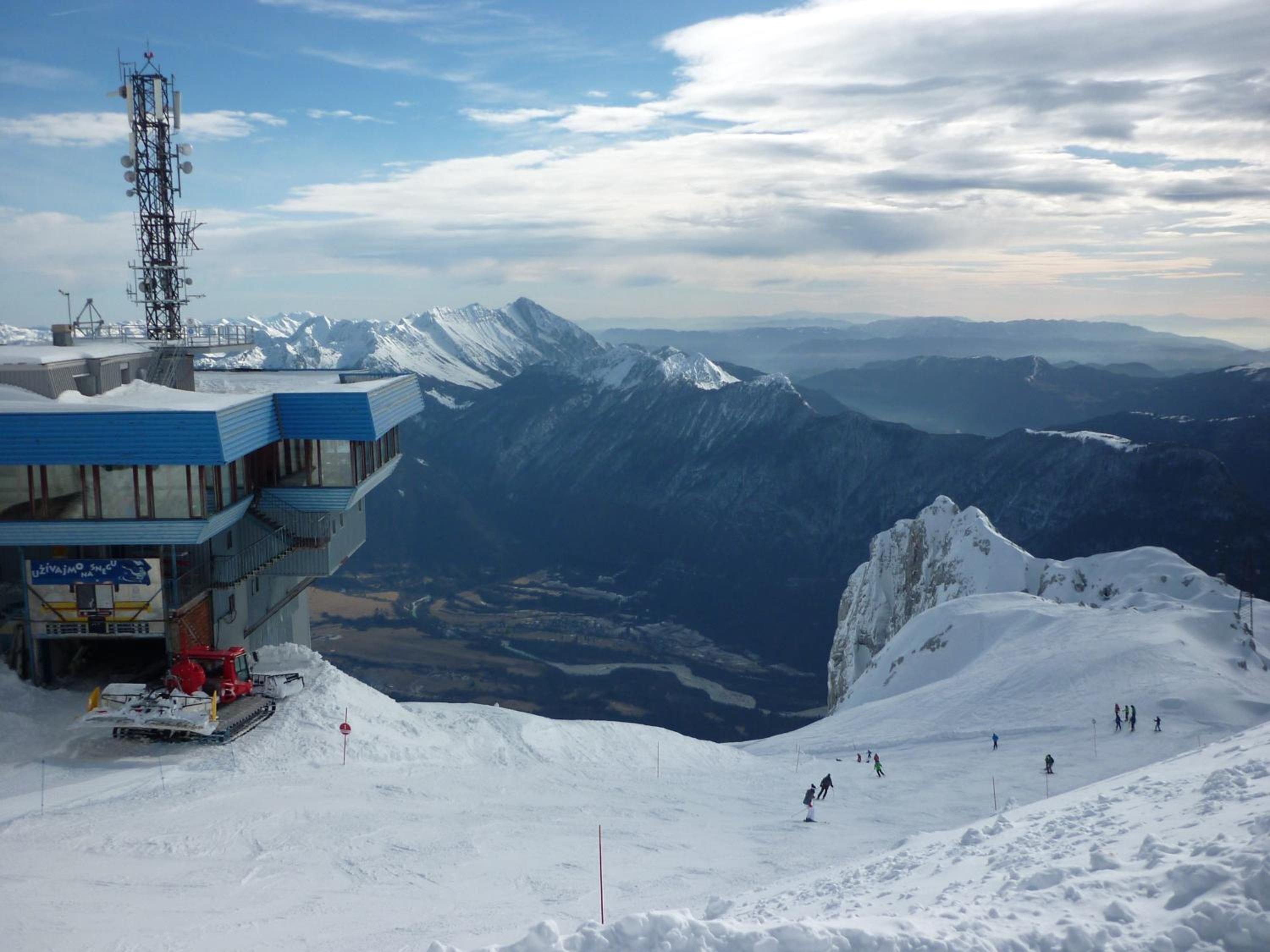 Montanha coberta de neve com um teleférico e um edifício com telhado azul.