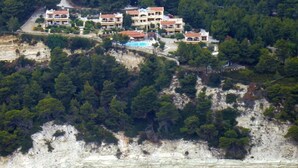 Um hotel à beira-mar com vários edifícios, piscina e um areal rochoso.