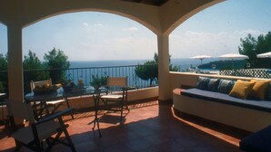 Uma área externa coberta com terraço, assentos e vista para o mar.