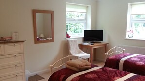 Quarto com duas camas, penteadeira, cadeira, escrivaninha com TV e janelas com vista para áreas verdes.